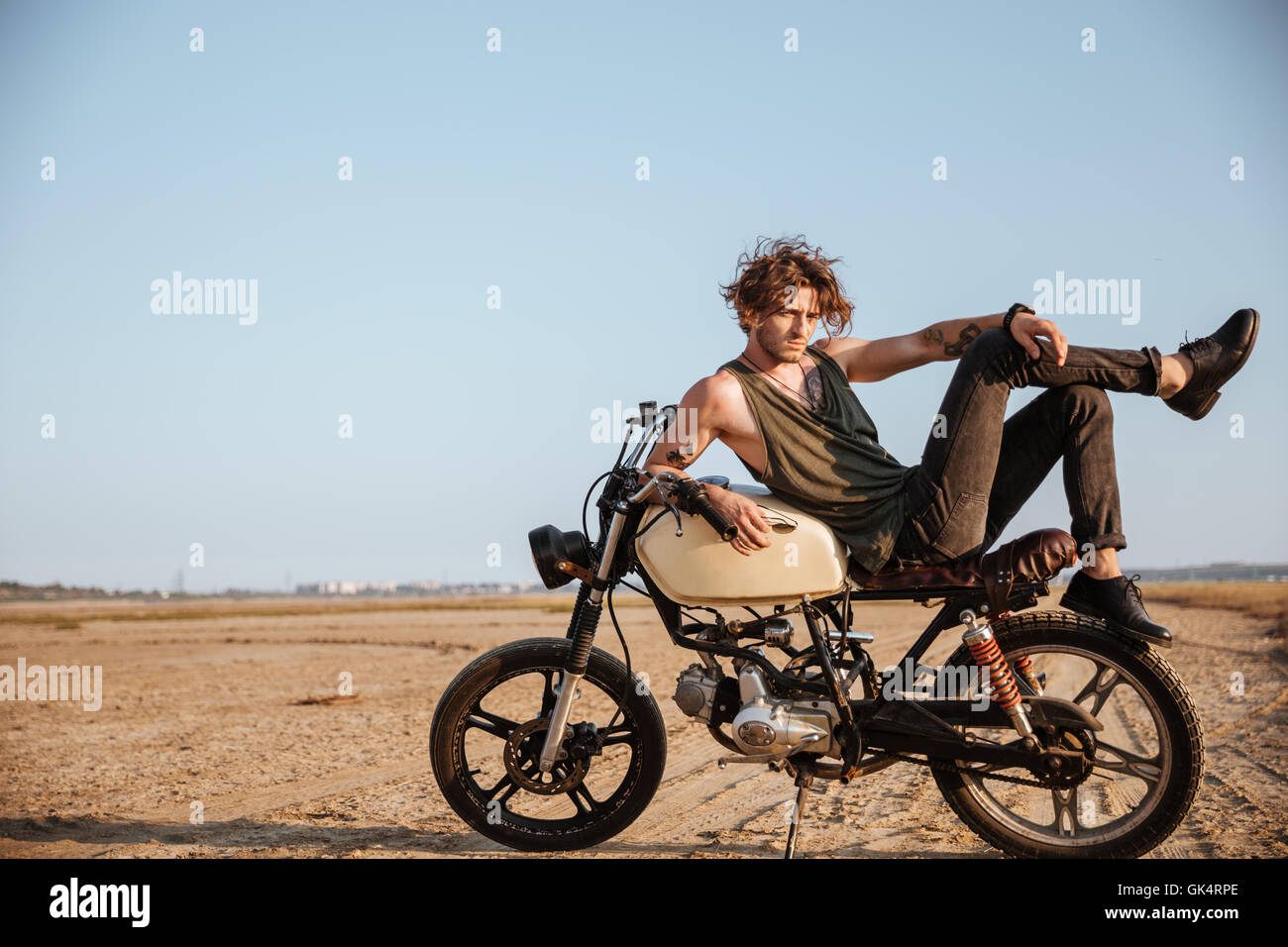 Young brutal man laying on his motorcycle in the desert and posing ...