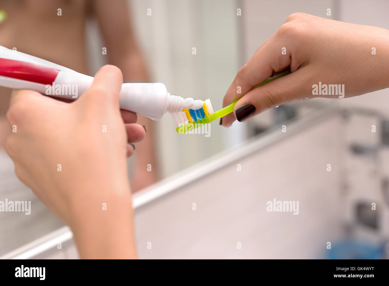 Hands holding a toothbrush and placing toothpaste on it in front of ...