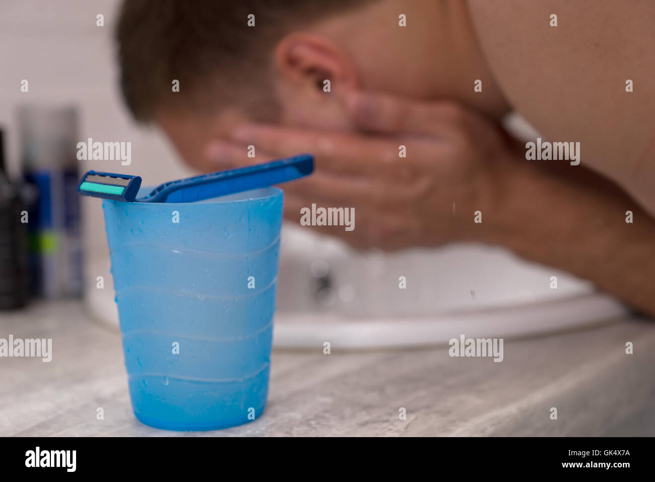 Cup with a razer on it and man spraying water on his face after shaving ...