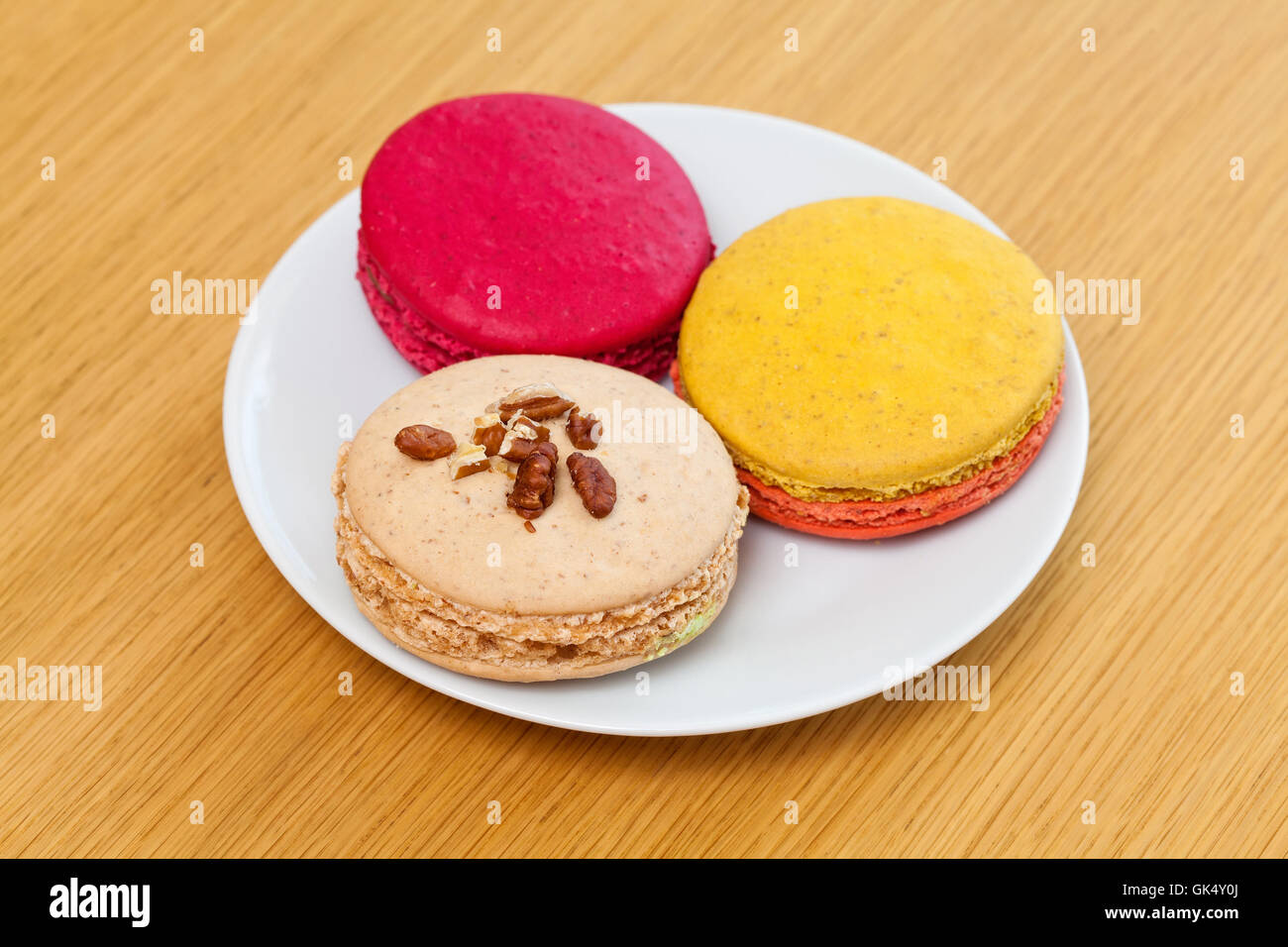 Three traditional french colorful macarons on plate, wooden background ...