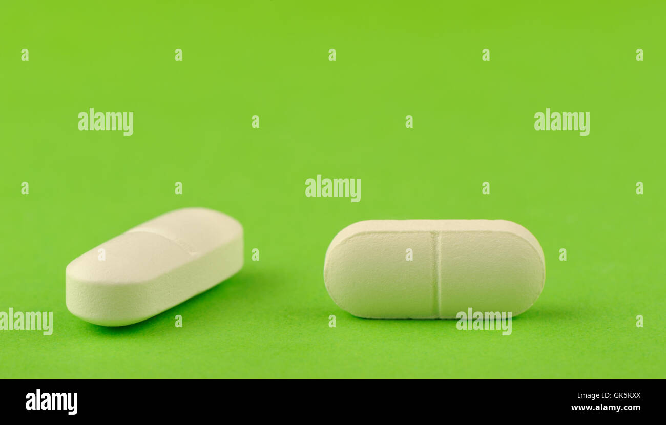Two white tablet on a green background Stock Photo - Alamy