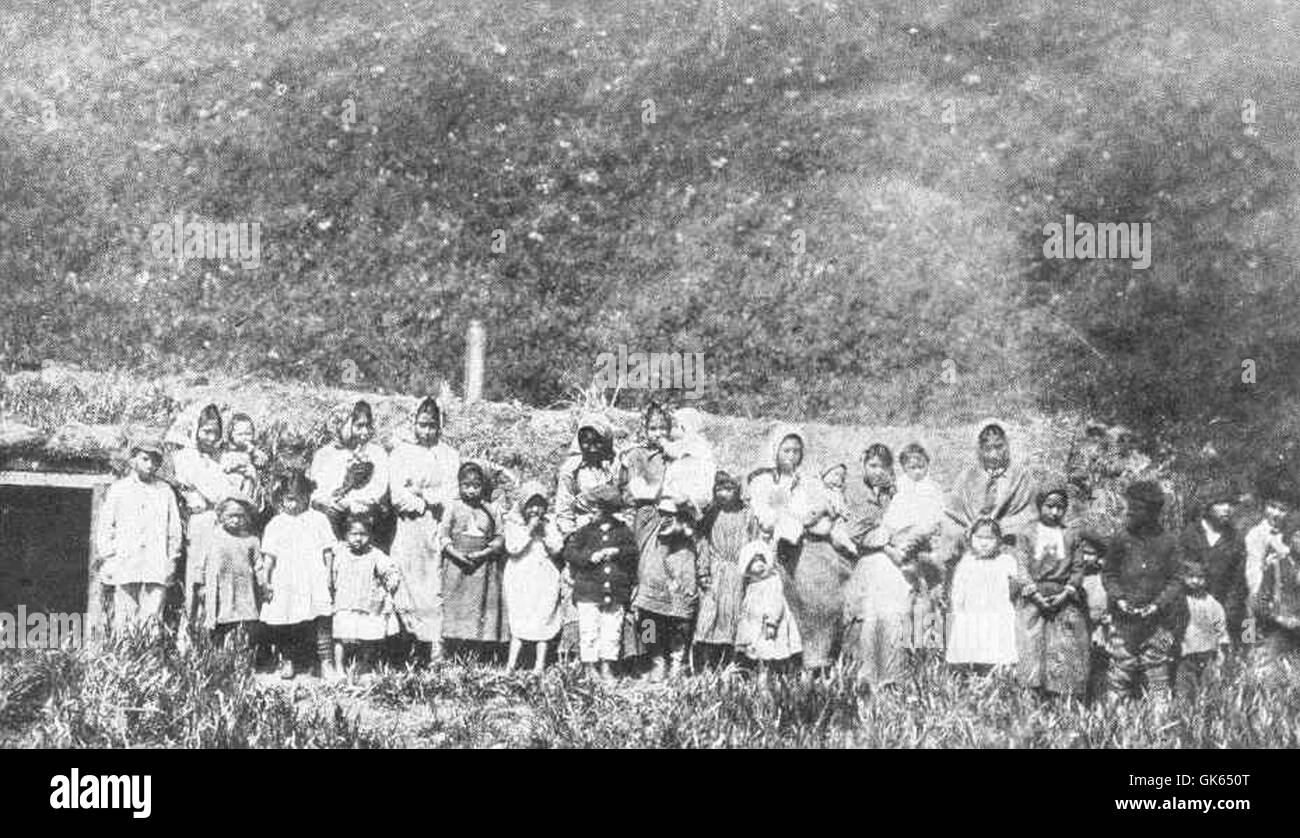 Akutan Aleuts standing before a traditional barabara or sod hut in ...