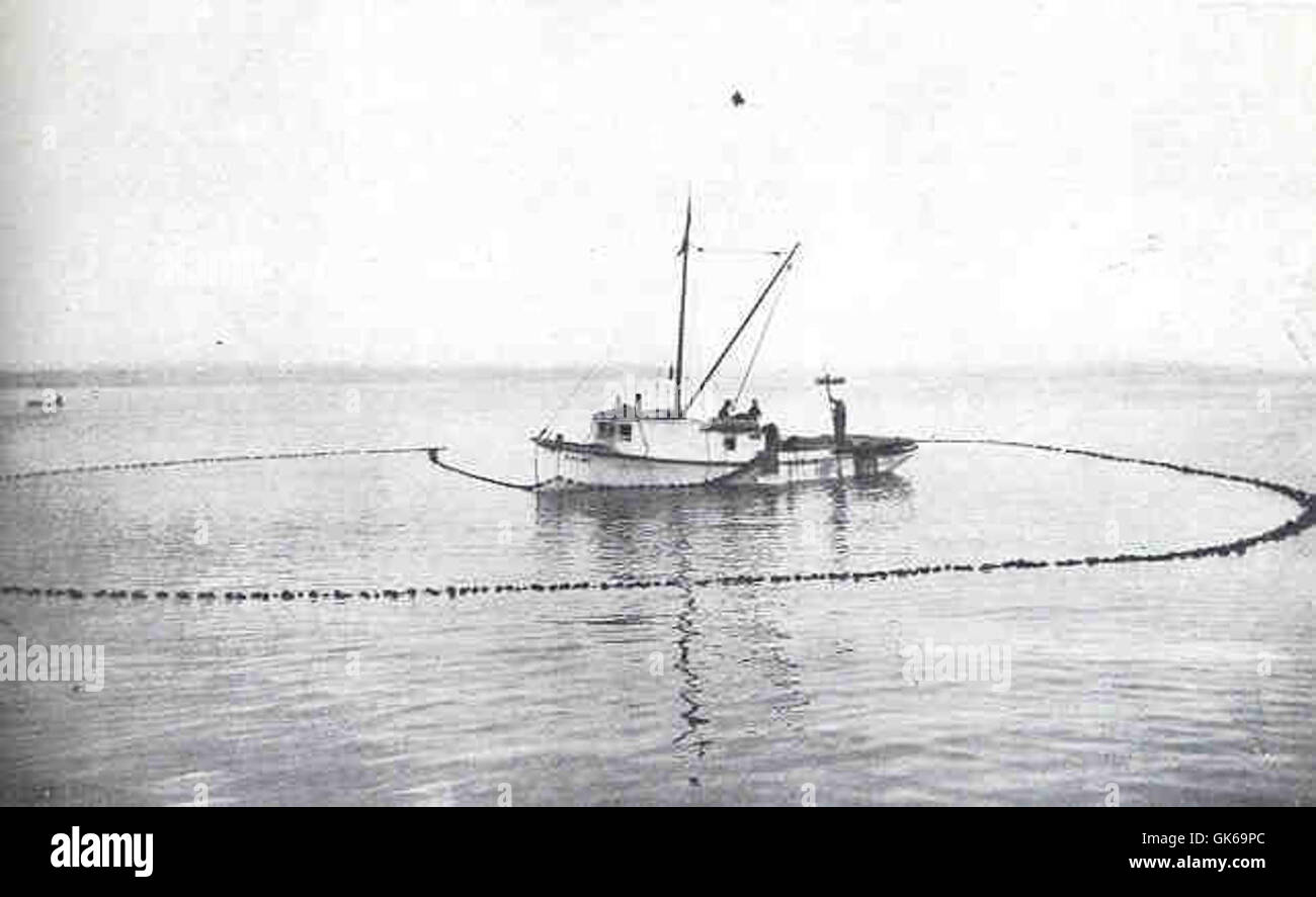 A purse seiner fishing vessel is depicted hauling in its net, a method ...