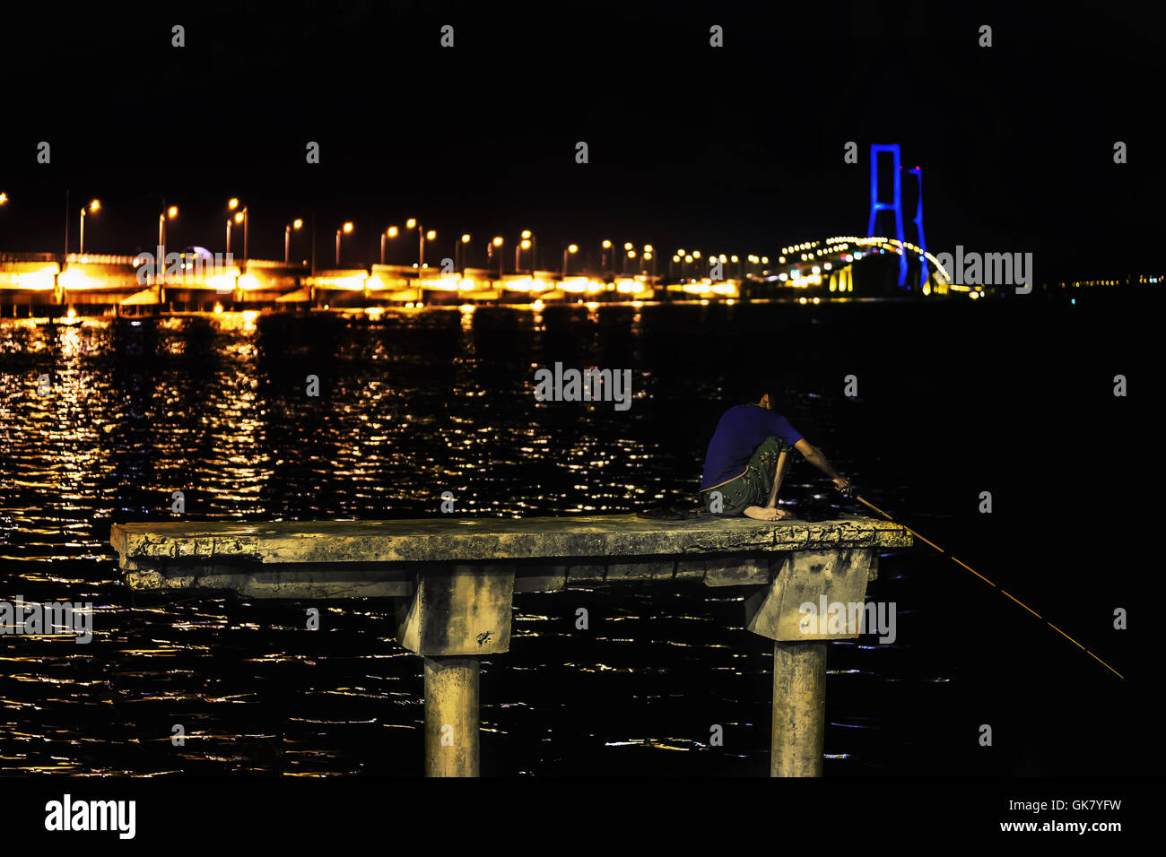 Fisherman on a concrete pylon catch fish at night. In backround ...
