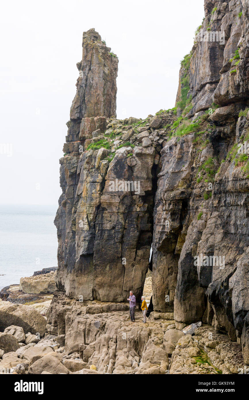 Two walkers explore the vertical limestone cliffs near St Govans Chapel ...