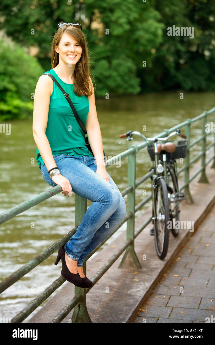 young brunette woman sitting on railing next to river Stock Photo - Alamy