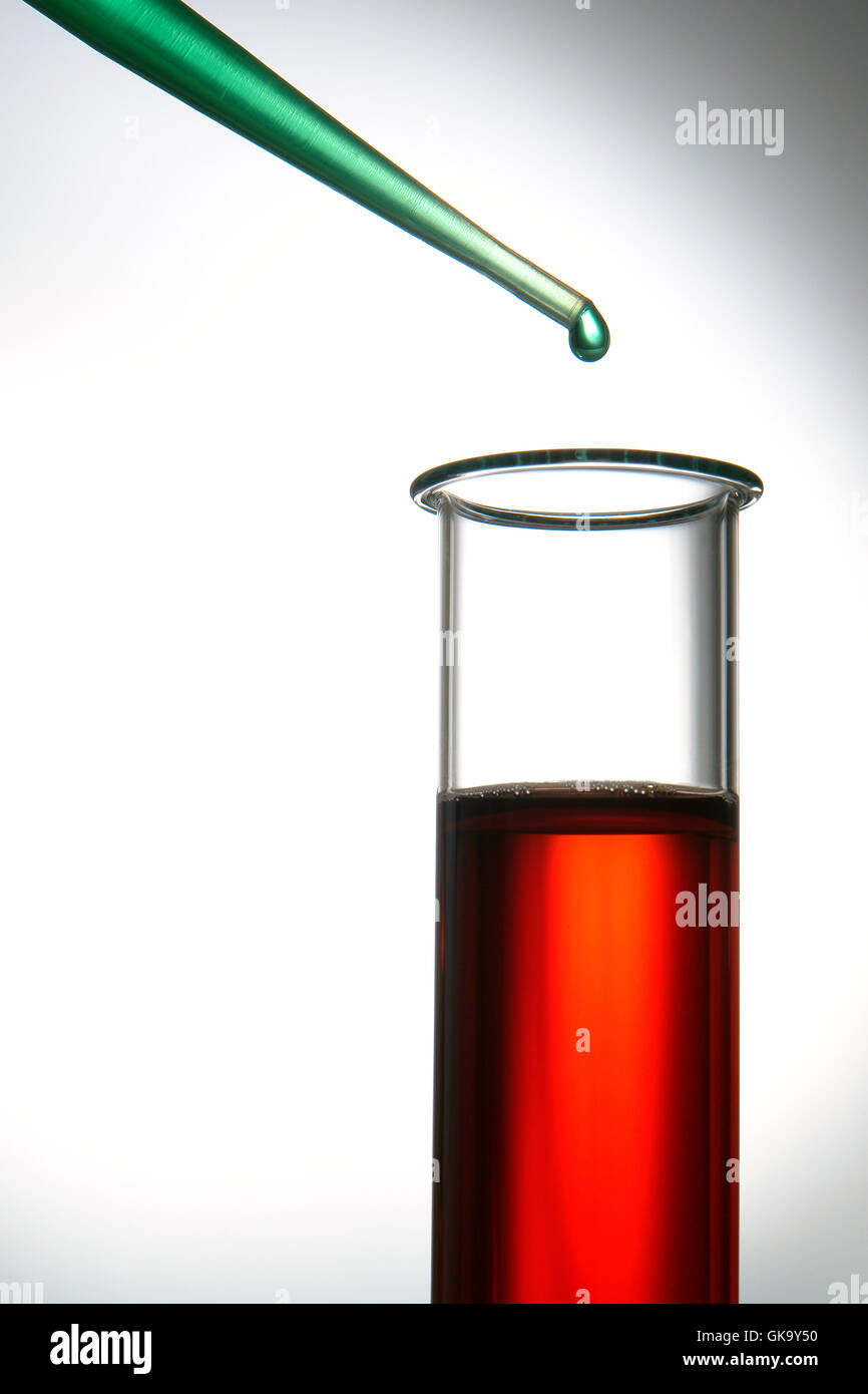 Drop of liquid hanging out of a laboratory pipette filled with green ...