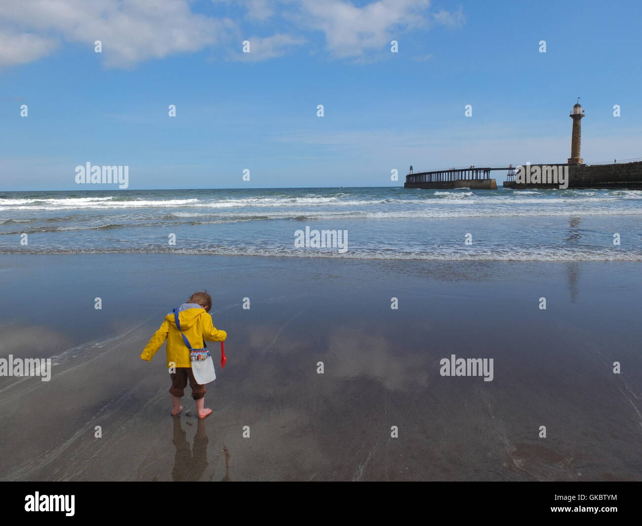 Toddler boy paddling in the sea on Whitby beach with lighthouse in ...