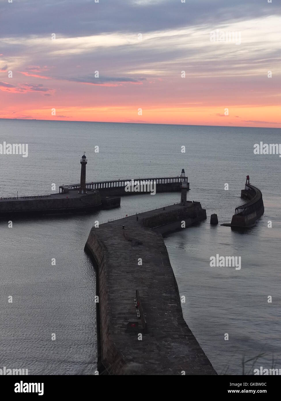 Pink skies of a sunset over the sea, lighthouse and pier at Whitby ...