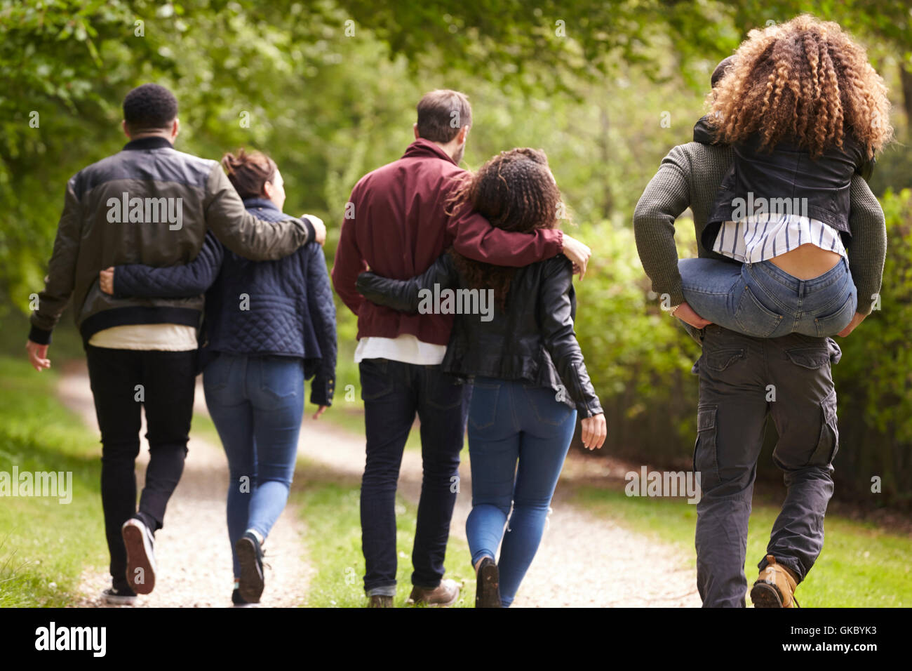 Young couples walk and piggyback in country lane, back view Stock Photo ...