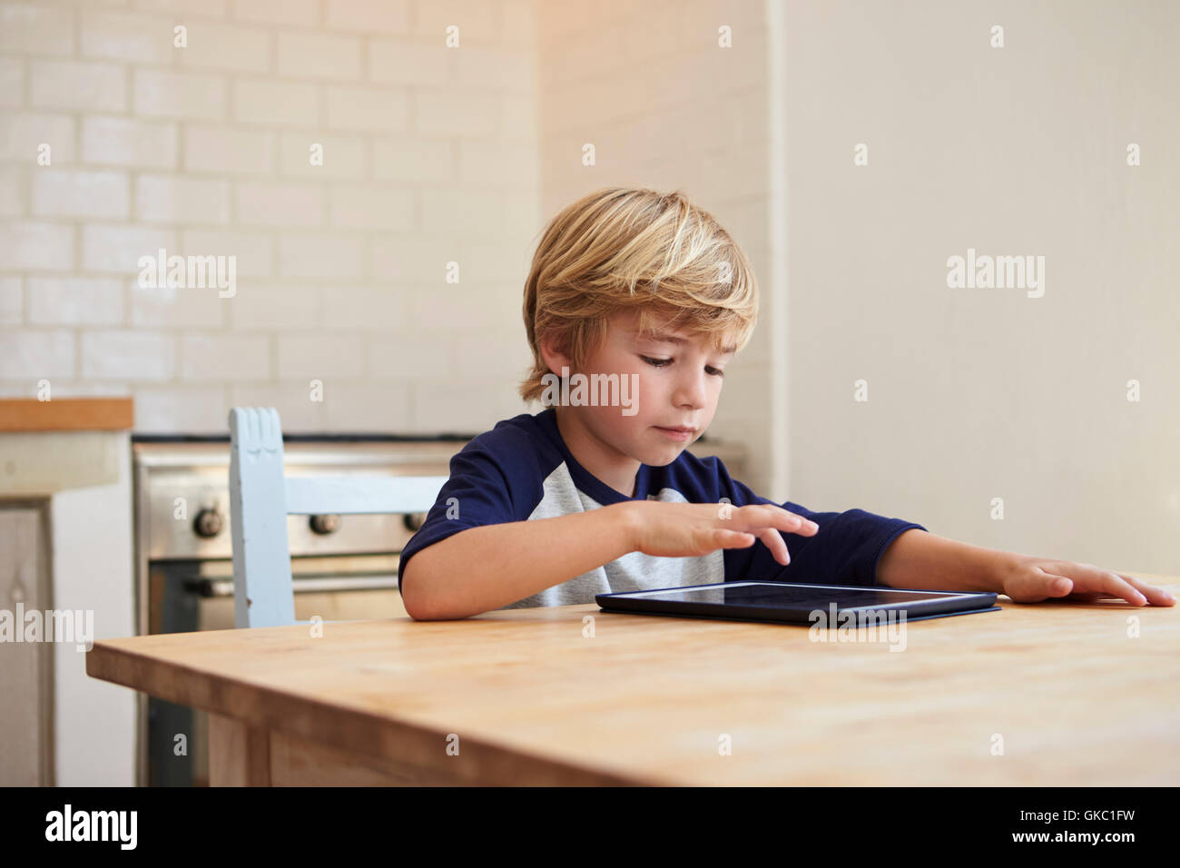Young boy using tablet computer at kitchen table Stock Photo - Alamy