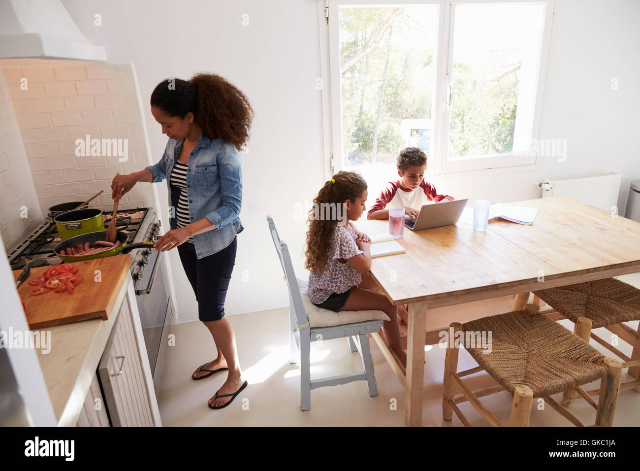 Mum cooking while kids work at kitchen table, elevated view Stock Photo ...