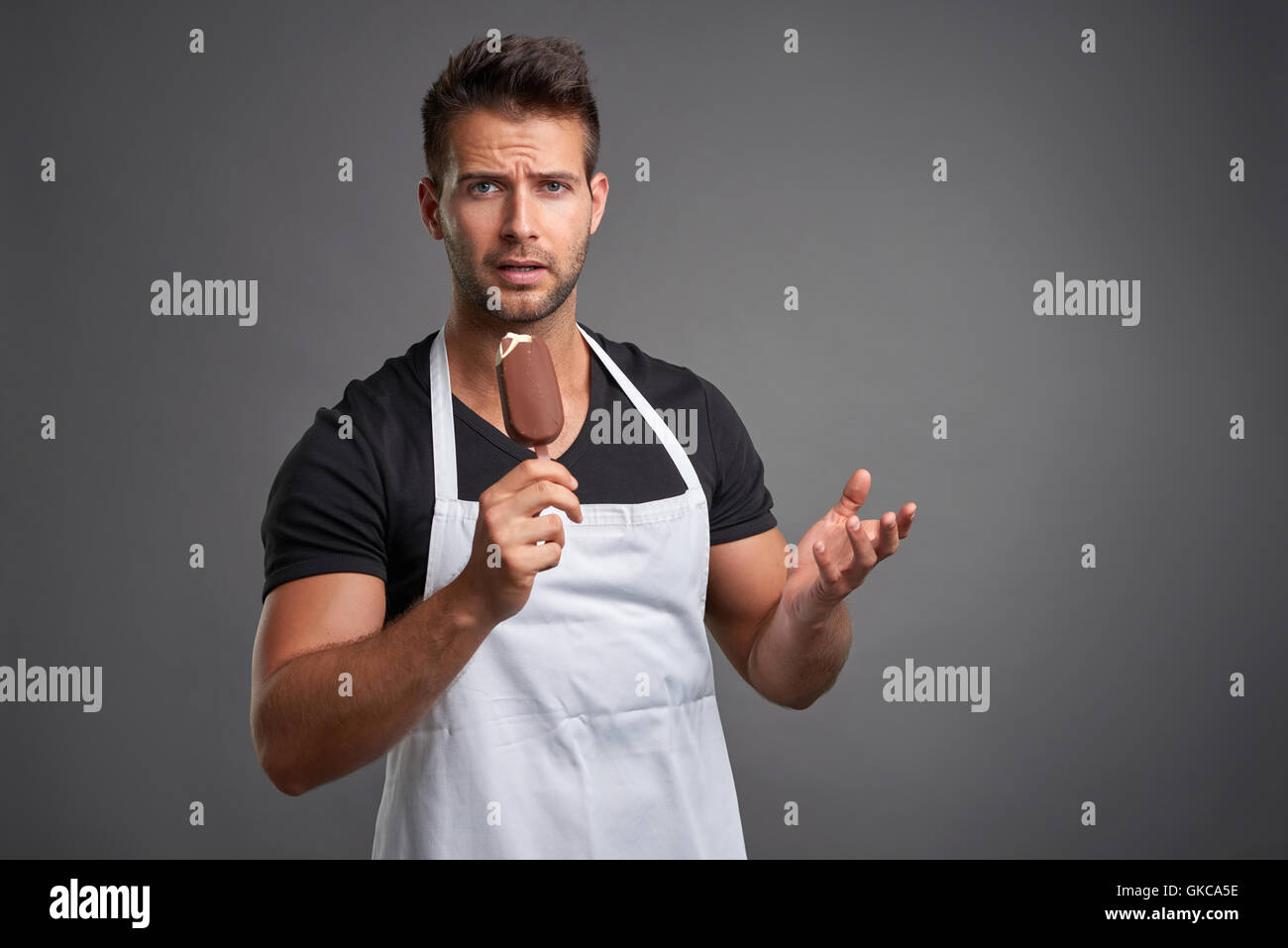 A handsome young barista man feeling confused while having an ice-cream ...