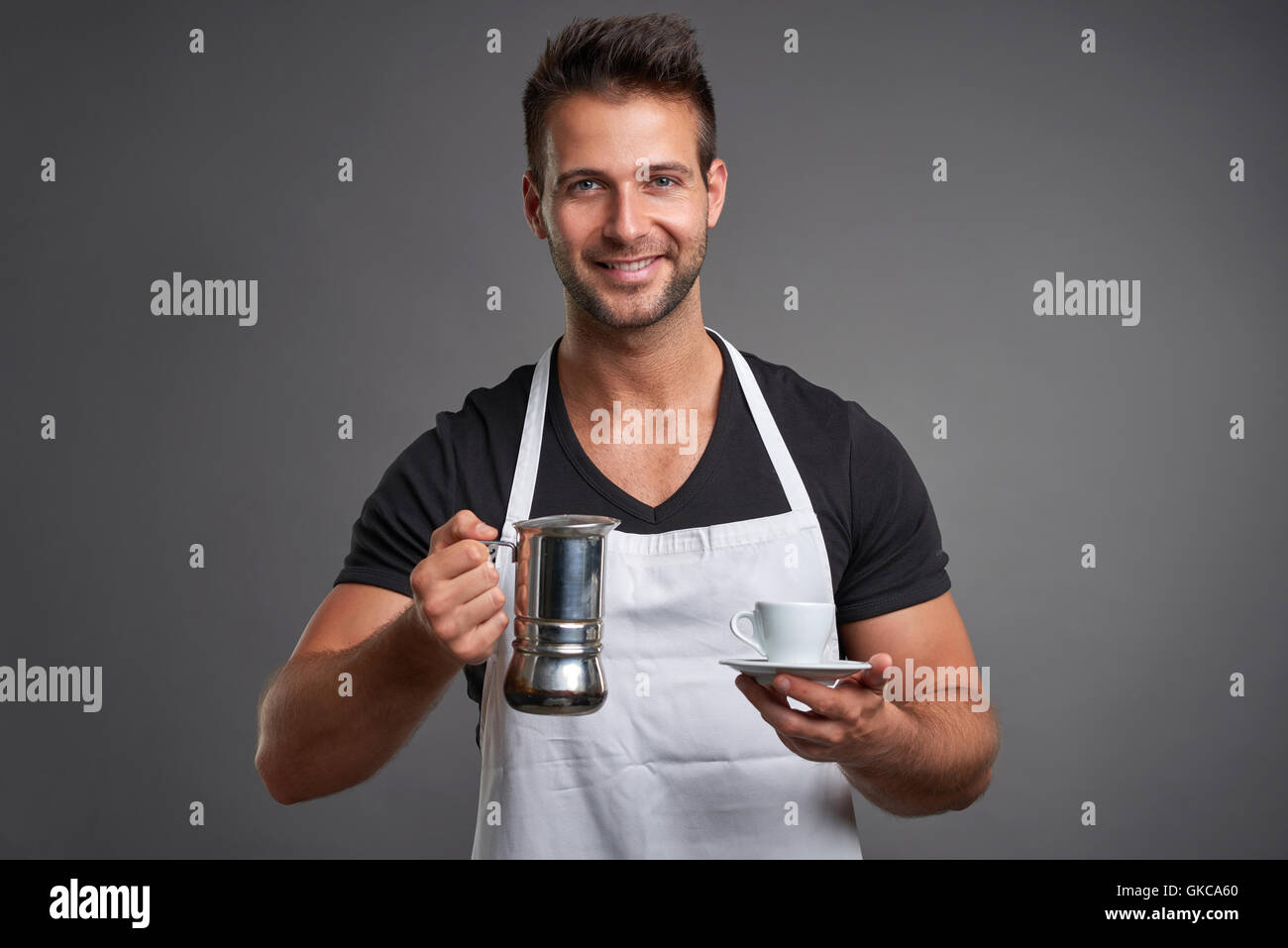 A young barista man smiling and holding a coffeecup and a percolator ...
