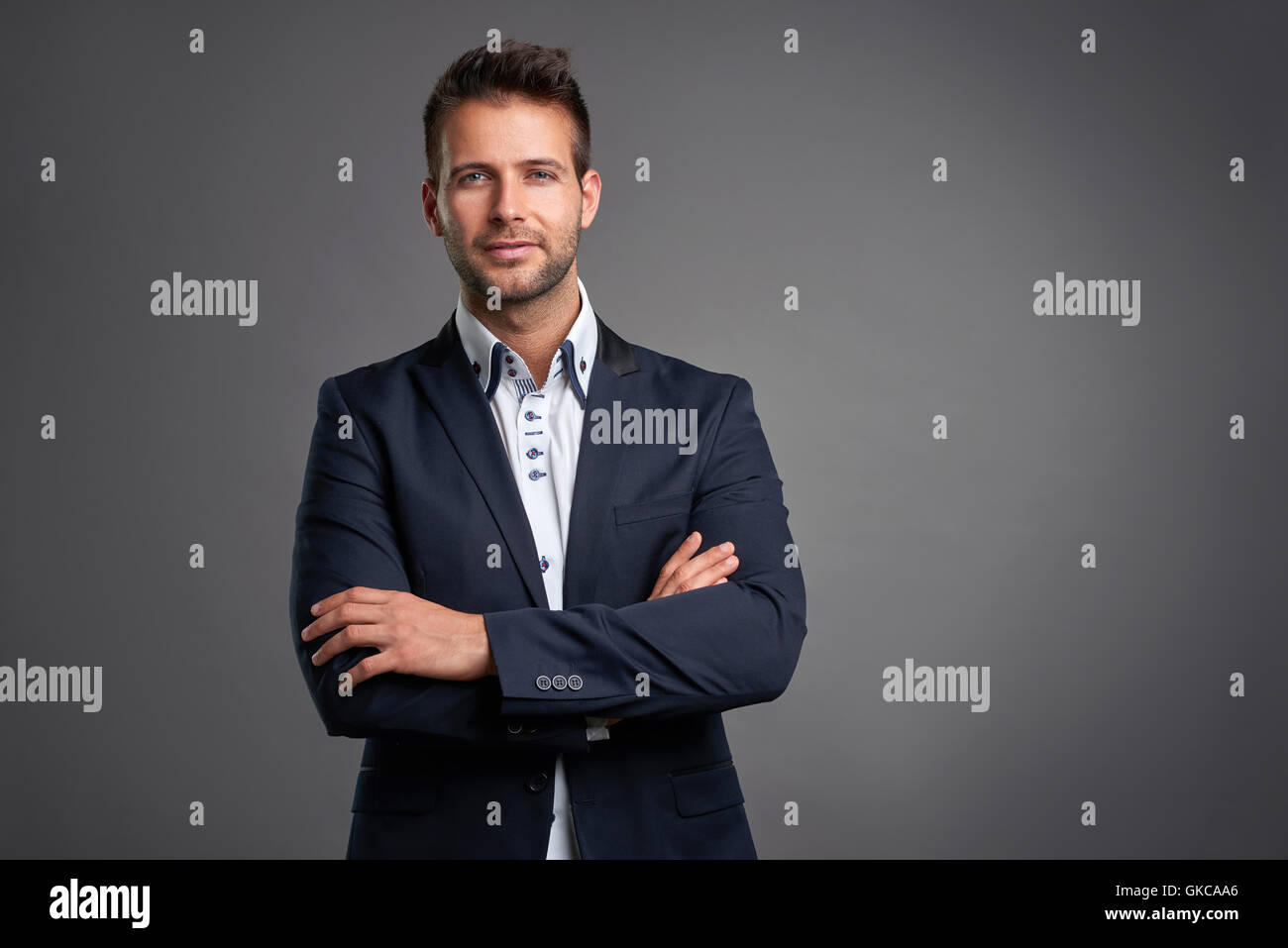 A confident elegant handsome young man standing in front of a grey ...