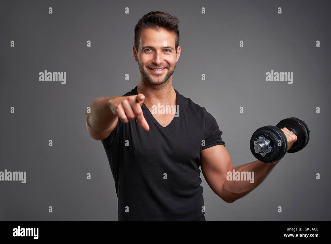 A handsome young man lifting weight smiling and pointing it to the ...