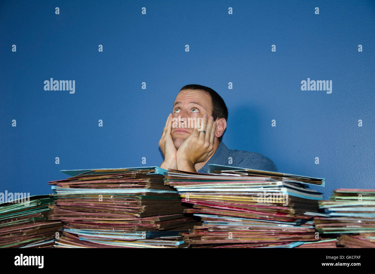 Man hiding behind piles files looking up at the ceiling. Example of an ...