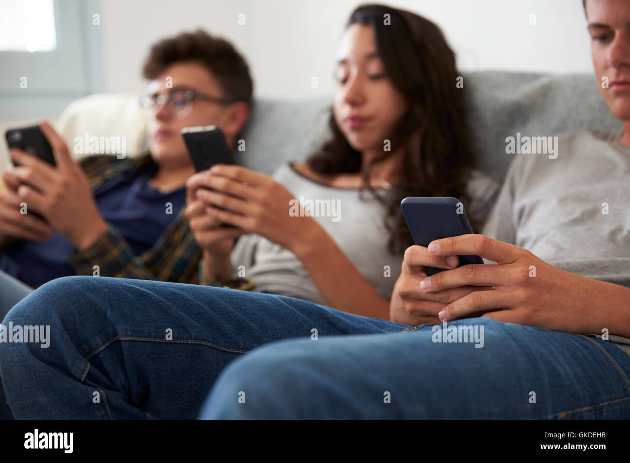 Three teenagers sitting together using smartphones at home Stock Photo ...