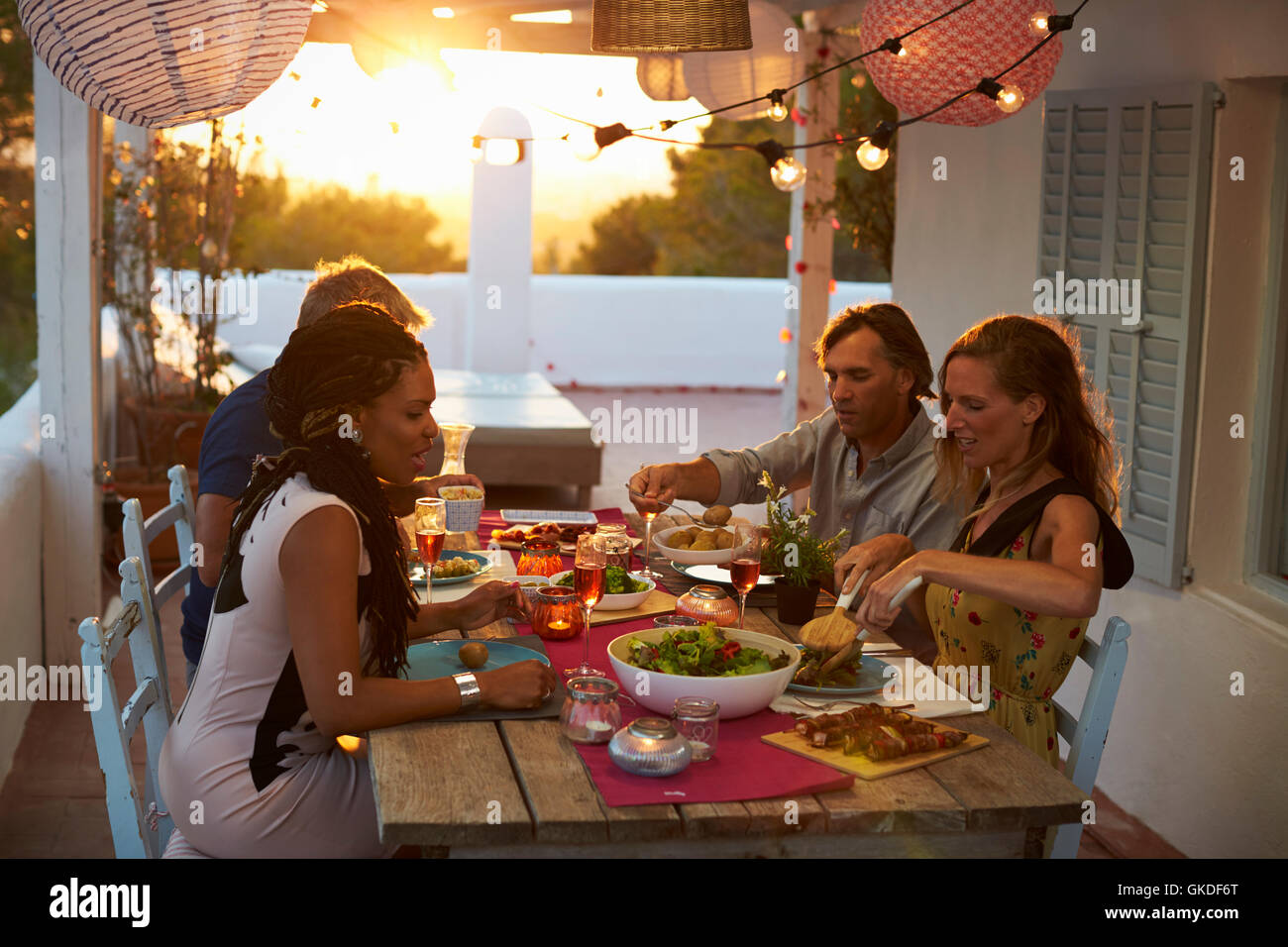 Two couples eating dinner at a table on a rooftop terrace Stock Photo ...