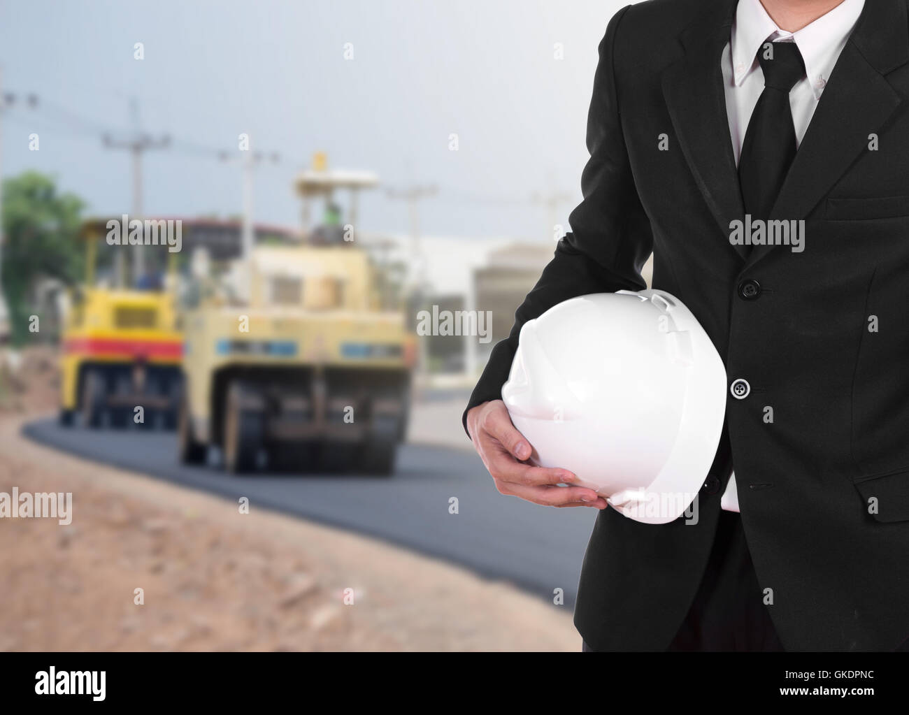 engineer in suit holding helmet with asphalt road under construction ...