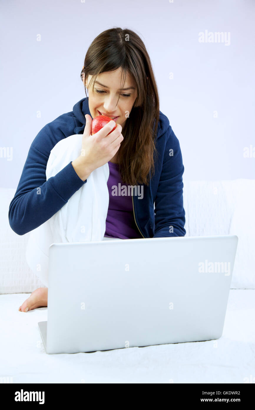 Woman smiling eats apple sitting in front of computer Stock Photo - Alamy