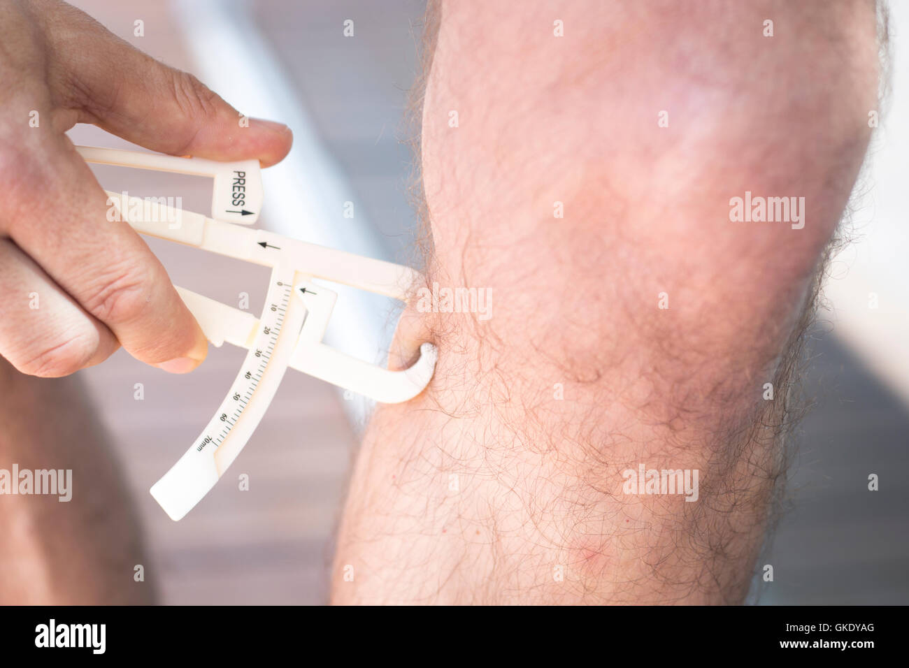 Slim attractive young man using fat caliper to measure bodyfat on leg ...