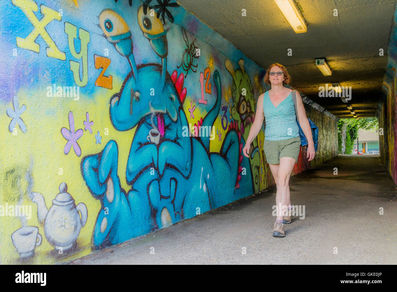 Woman walks through pedestrian underpass. graffiti style mural painted ...