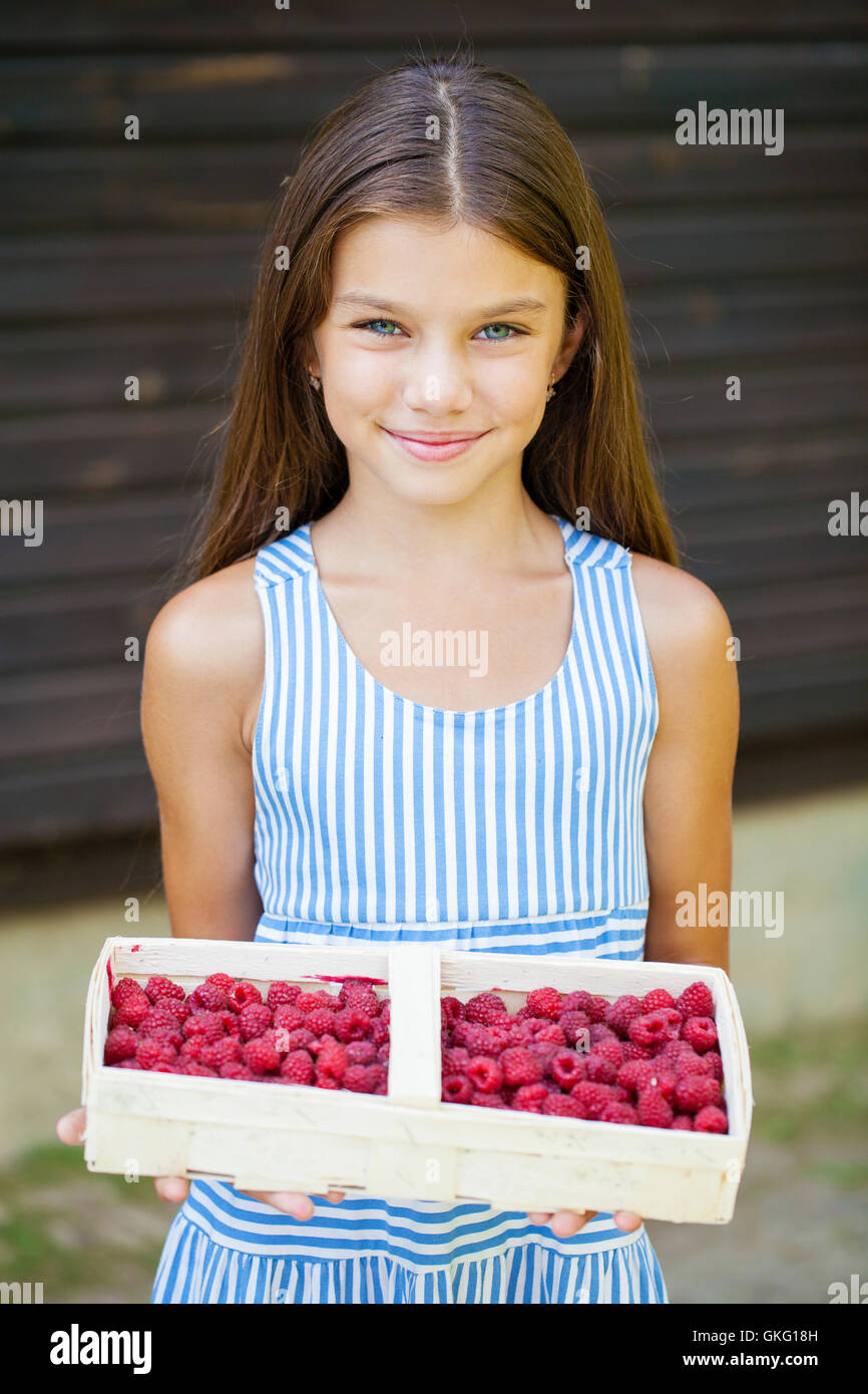 Beautiful brunette little girl holding a box with a raspberry, summer outdoors Stock Photo - Alamy