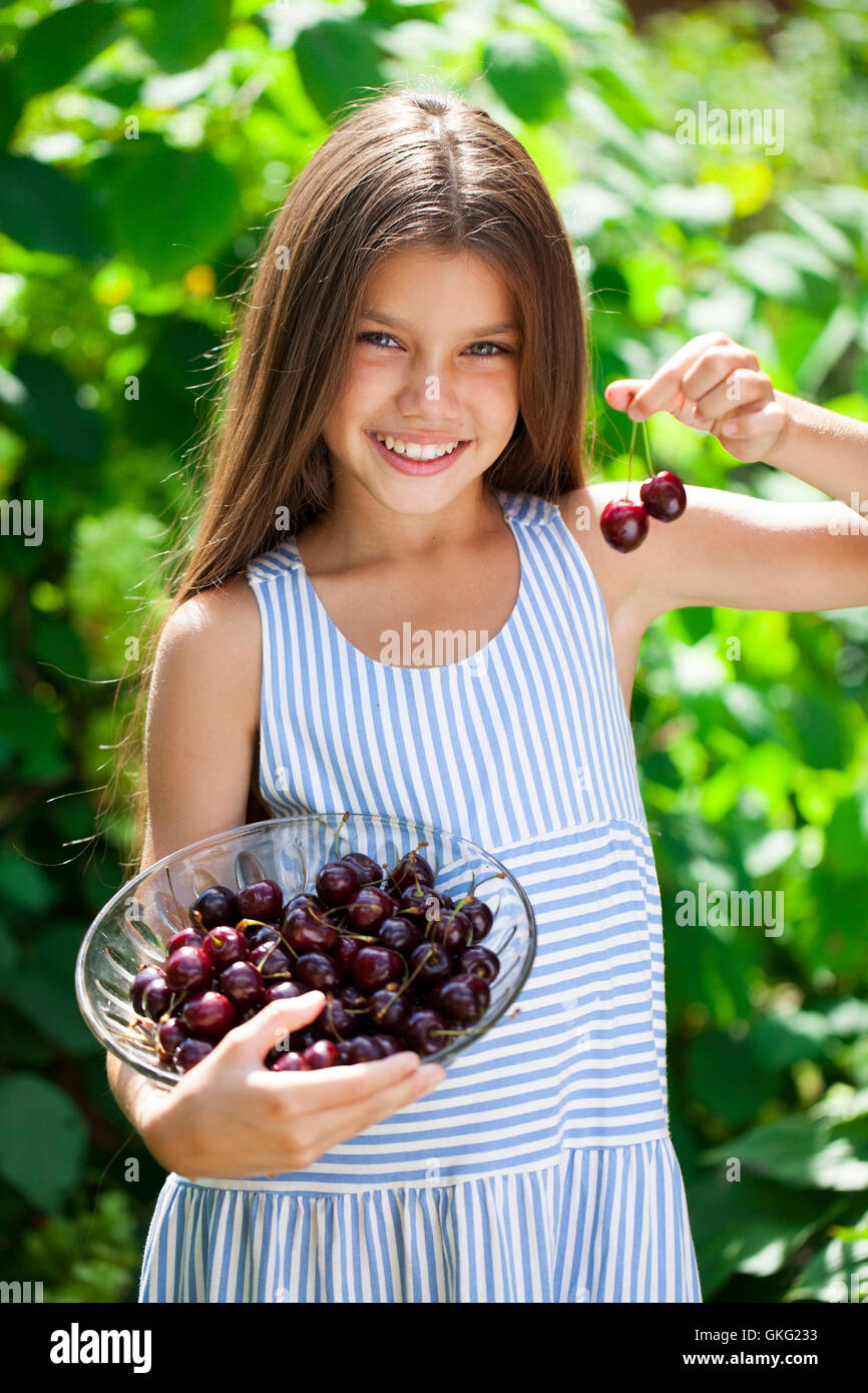 Beautiful brunette little girl holding a bowl of cherries in the garden ...