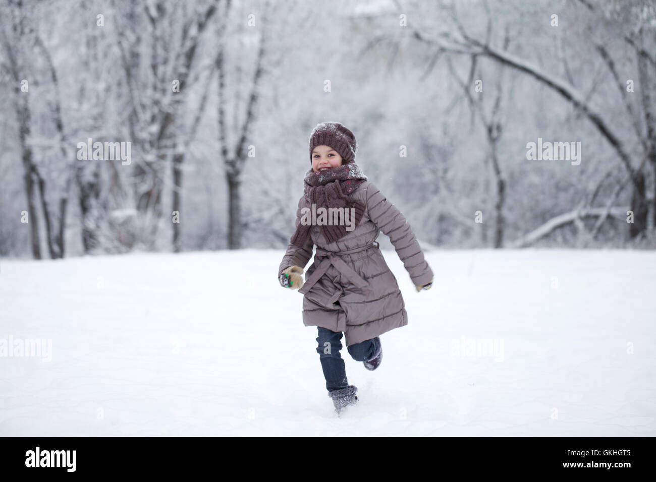 Little girl running on the background of snow covered winter park Stock ...
