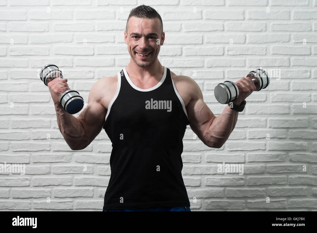 Young Man Working Out Biceps With Dumbbells On White Bricks Background ...