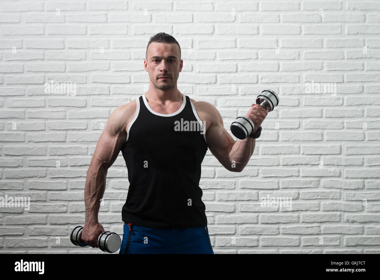 Bodybuilder Working Out Biceps With Dumbbells On White Bricks ...