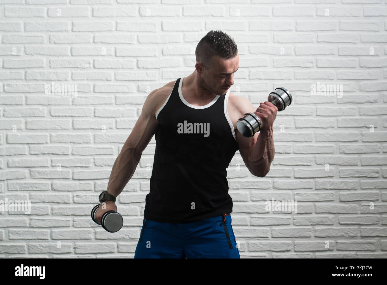 Young Man Working Out Biceps With Dumbbells On White Bricks Background ...
