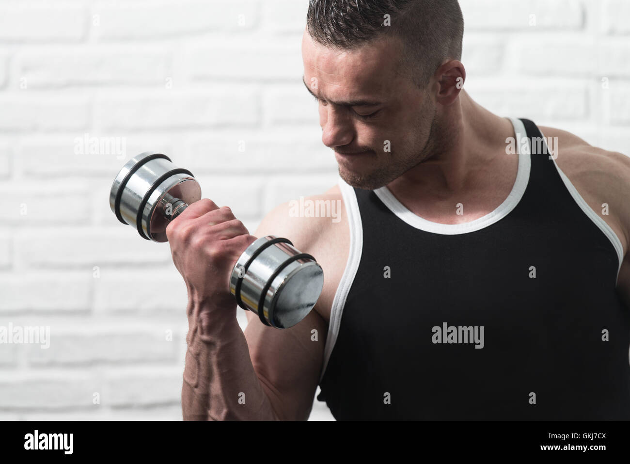 Bodybuilder Working Out Biceps With Dumbbells On White Bricks ...