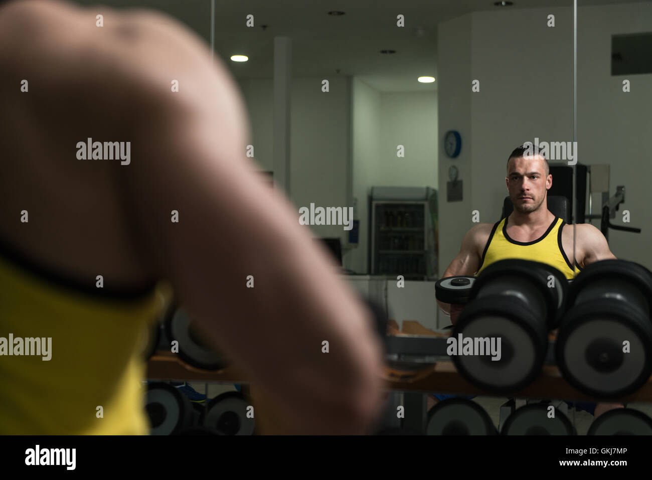 Young Strong Man In The Gym And Exercising Shoulders With Dumbbells At ...