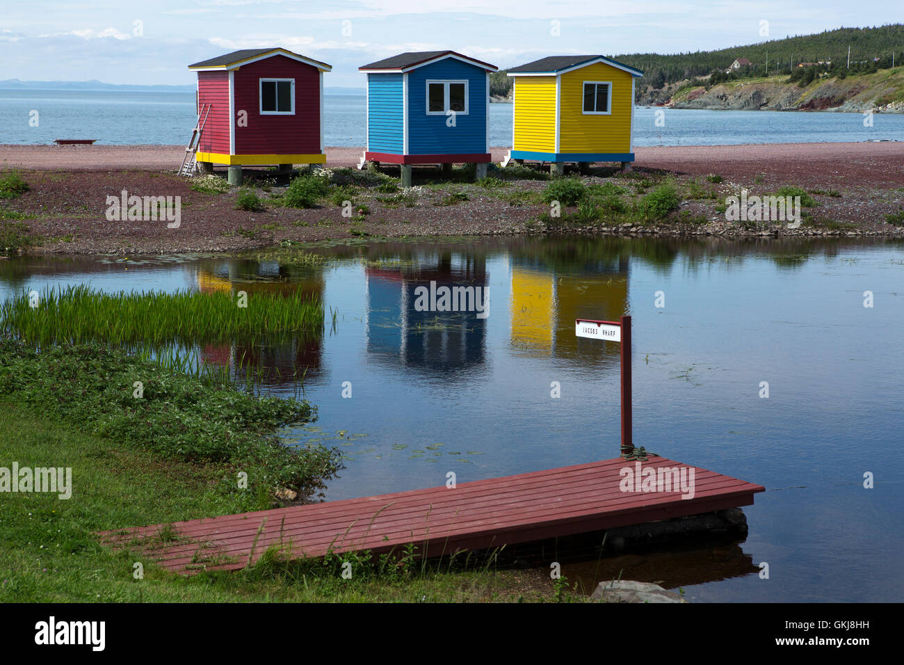 Colourfully painted cabins reflecting in a pond at Heart's Delight ...