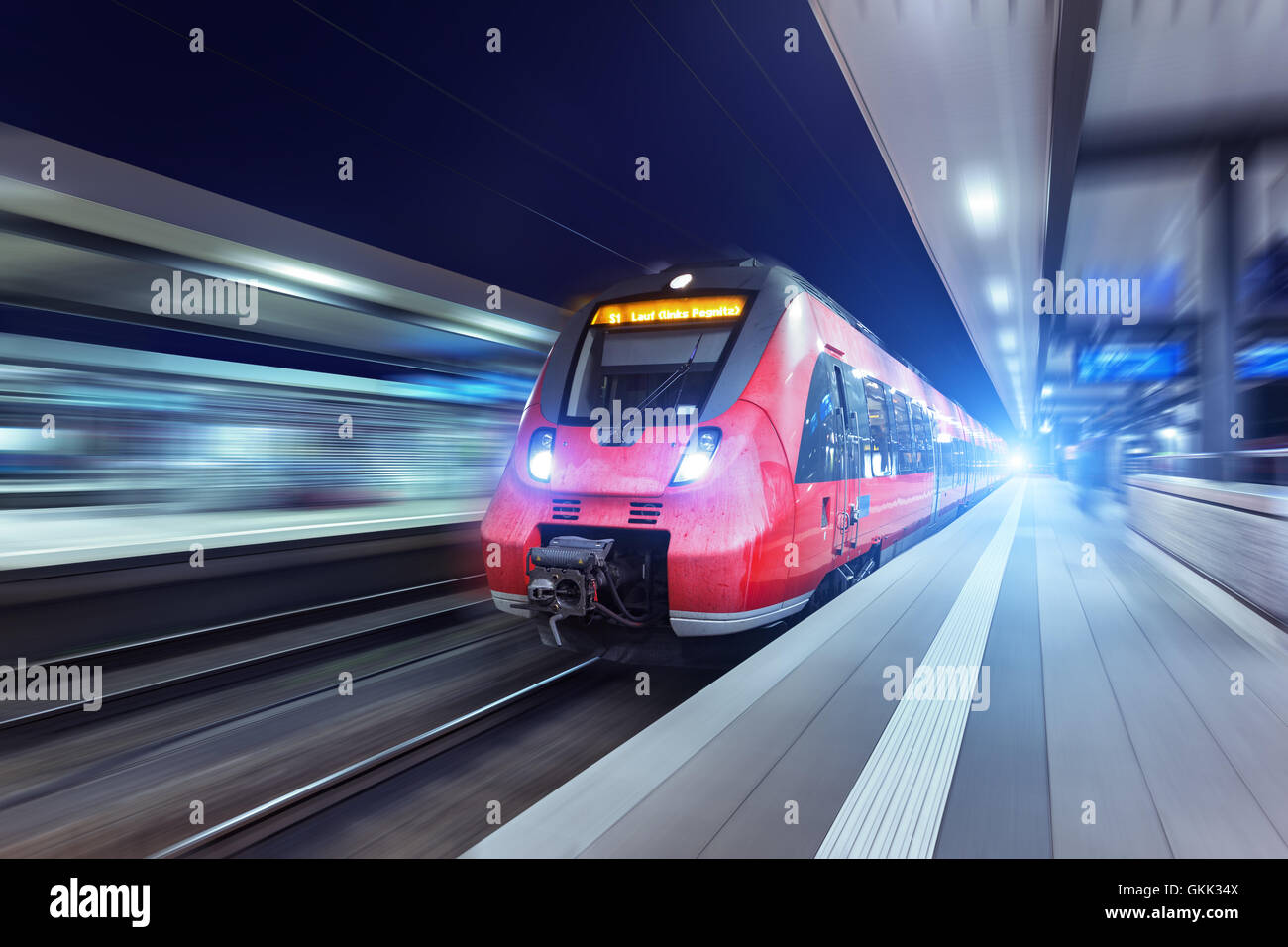 Modern high speed red passenger train moving through railway station at ...