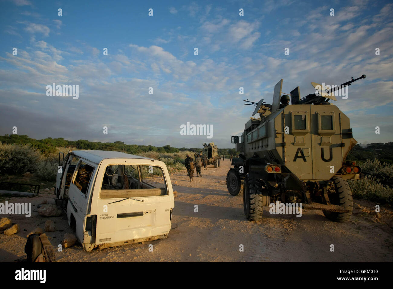 An AMISOM armored personnel carrier passes a destroyed vehicle in ...