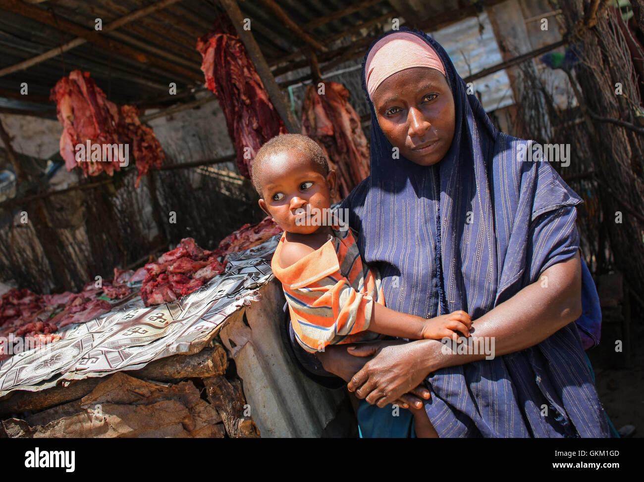 A Somali woman selling meat from a kiosk holds her child in a market in ...