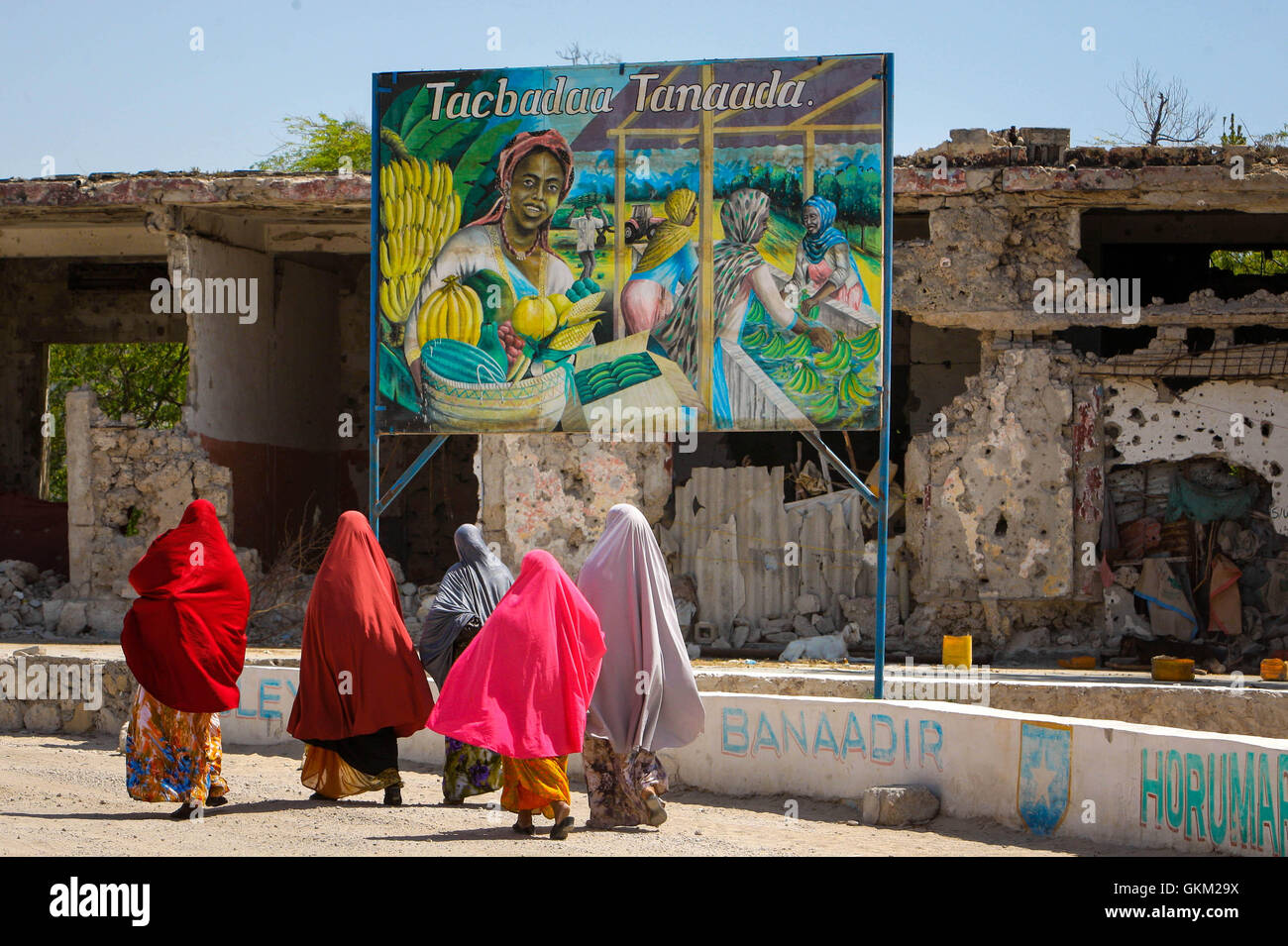 Somali women walk past a mural reading Cultivate to prosper in ...