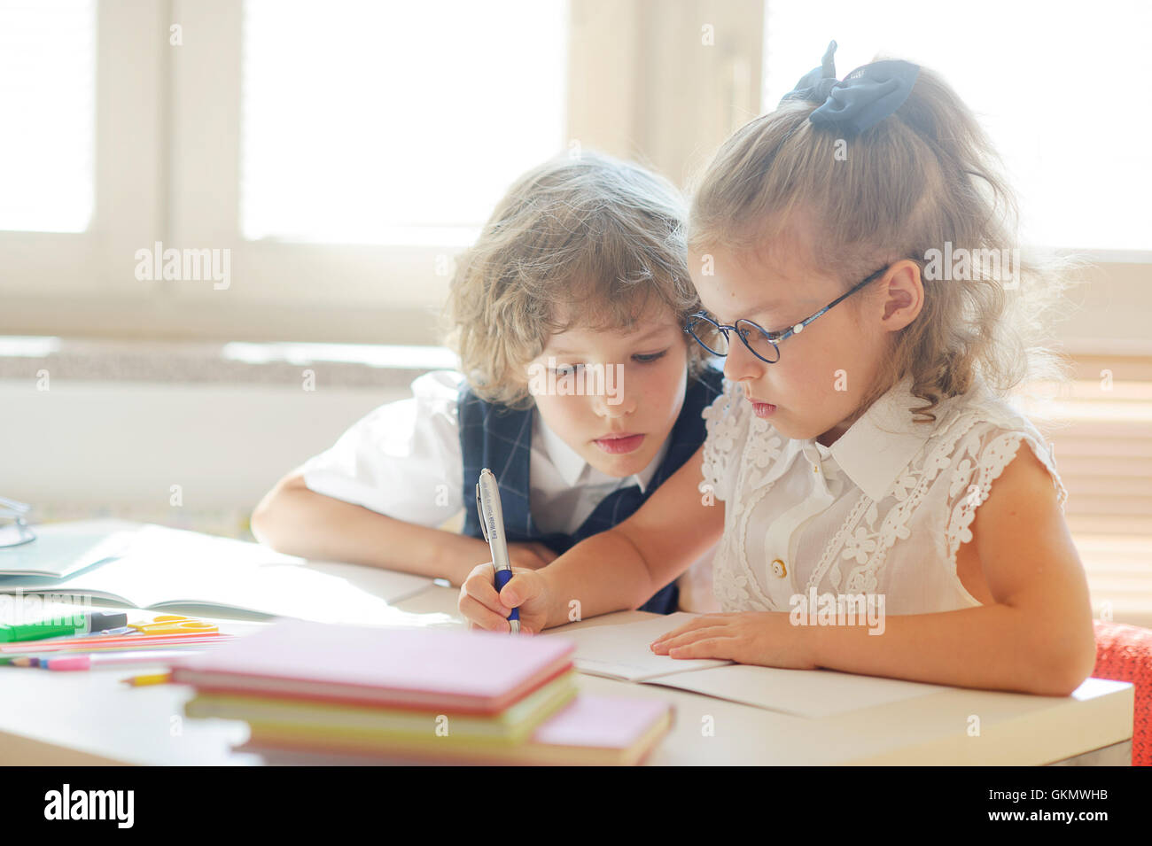 Two little classmate, boy and girl, are sitting at the same desk. This ...