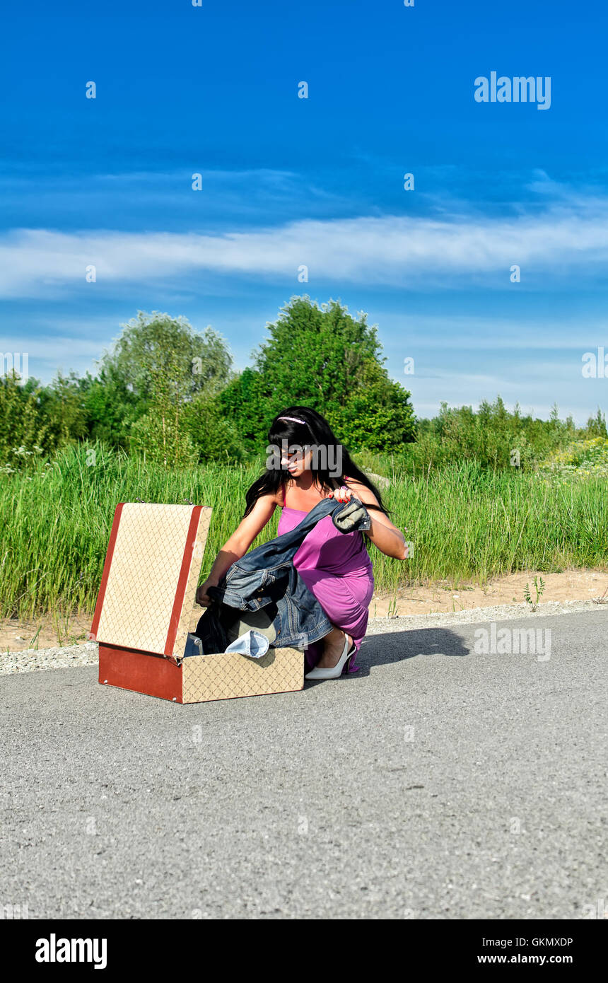 Woman on a road getting clothes from suitcase Stock Photo - Alamy