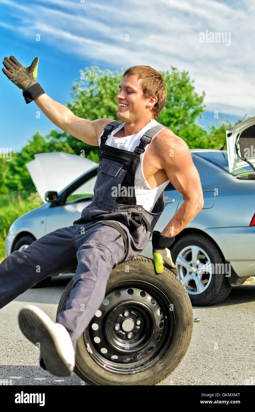 Portrait of laughing mechanic sitting on a tire on a road Stock Photo ...