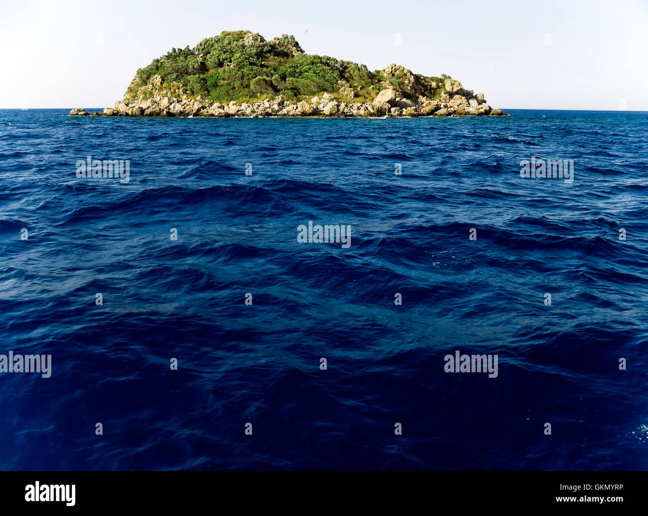 green island in the middle of the ocean waves on blue sky background ...