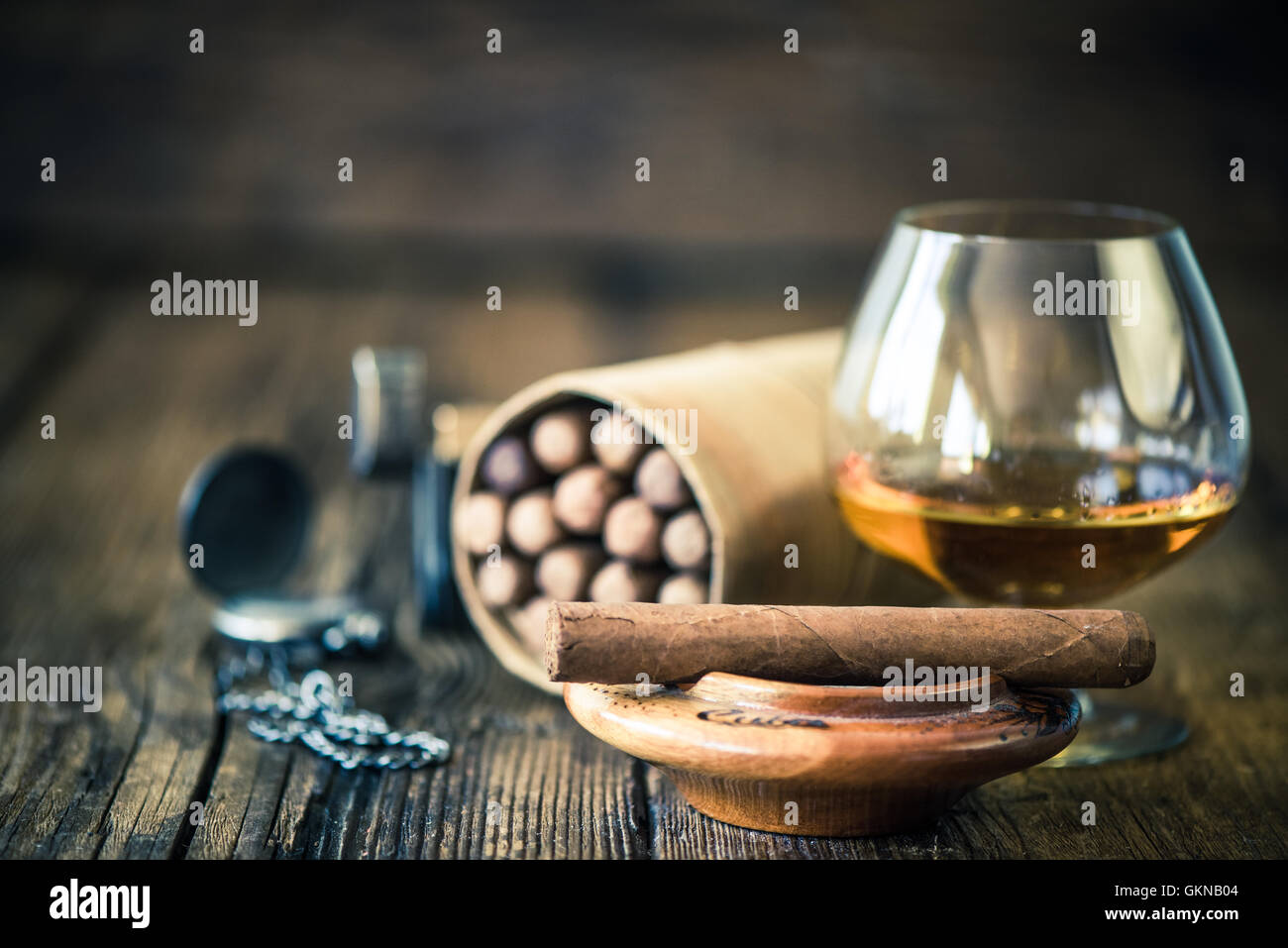 cuban cigar in ashtray on wooden table with glass of cognac or rum ...