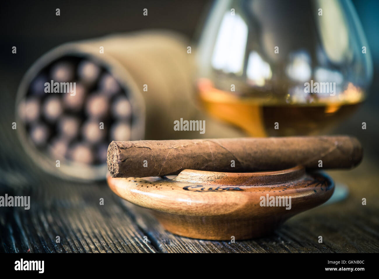 cuban cigar in ashtray on wooden table with glass of cognac or rum ...