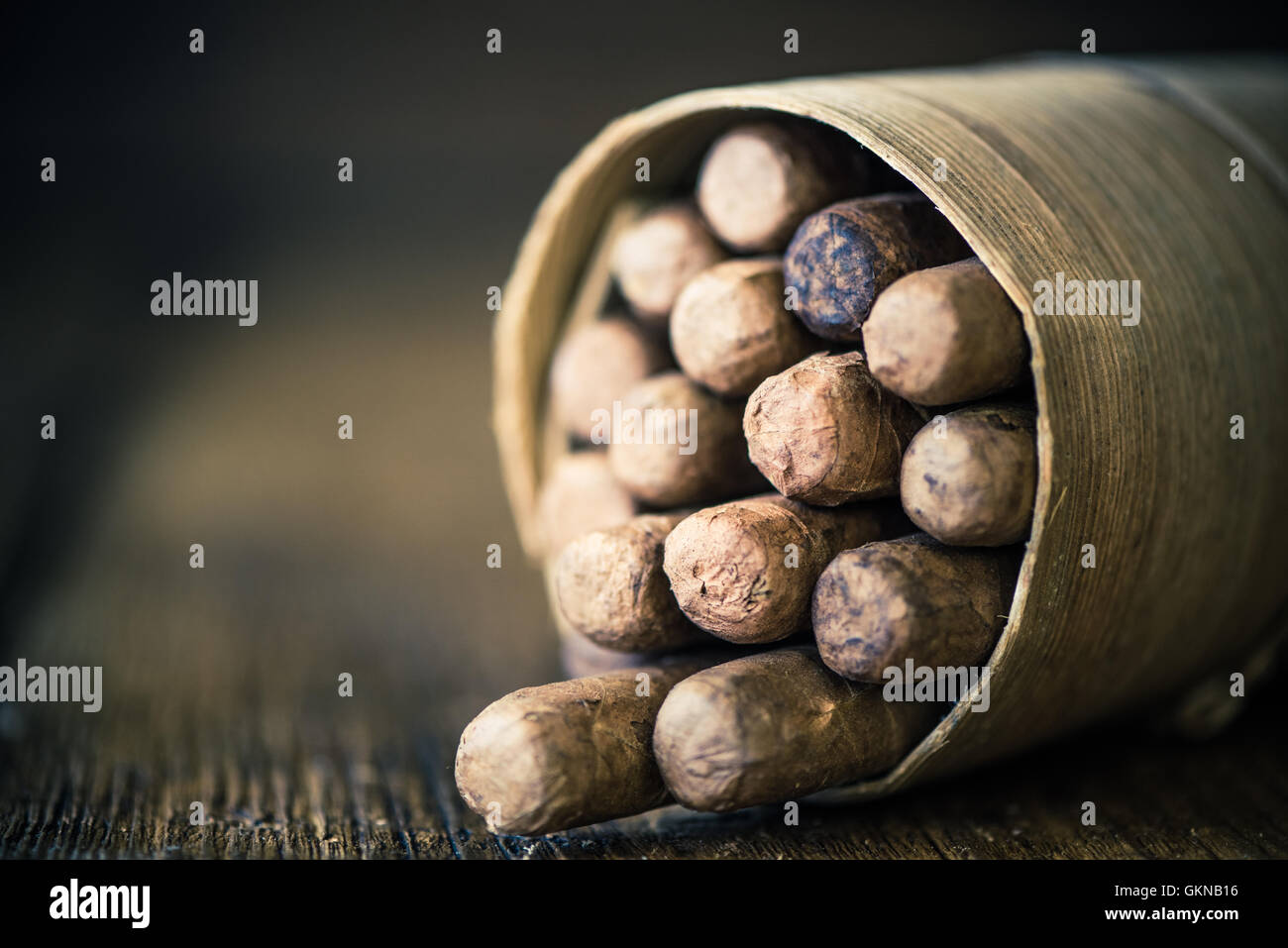 bunch of cigars wrapped in palm leaf on wooden table, moody and dark ...
