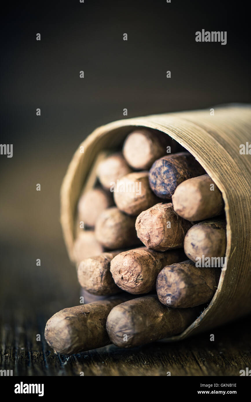 bunch of cigars wrapped in palm leaf on wooden table, moody and dark ...