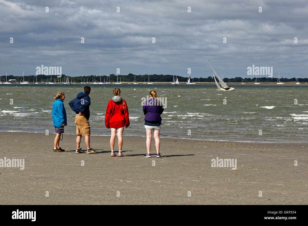 Walkers on the beach watch a sailing boat heeled over, decks awash and ...