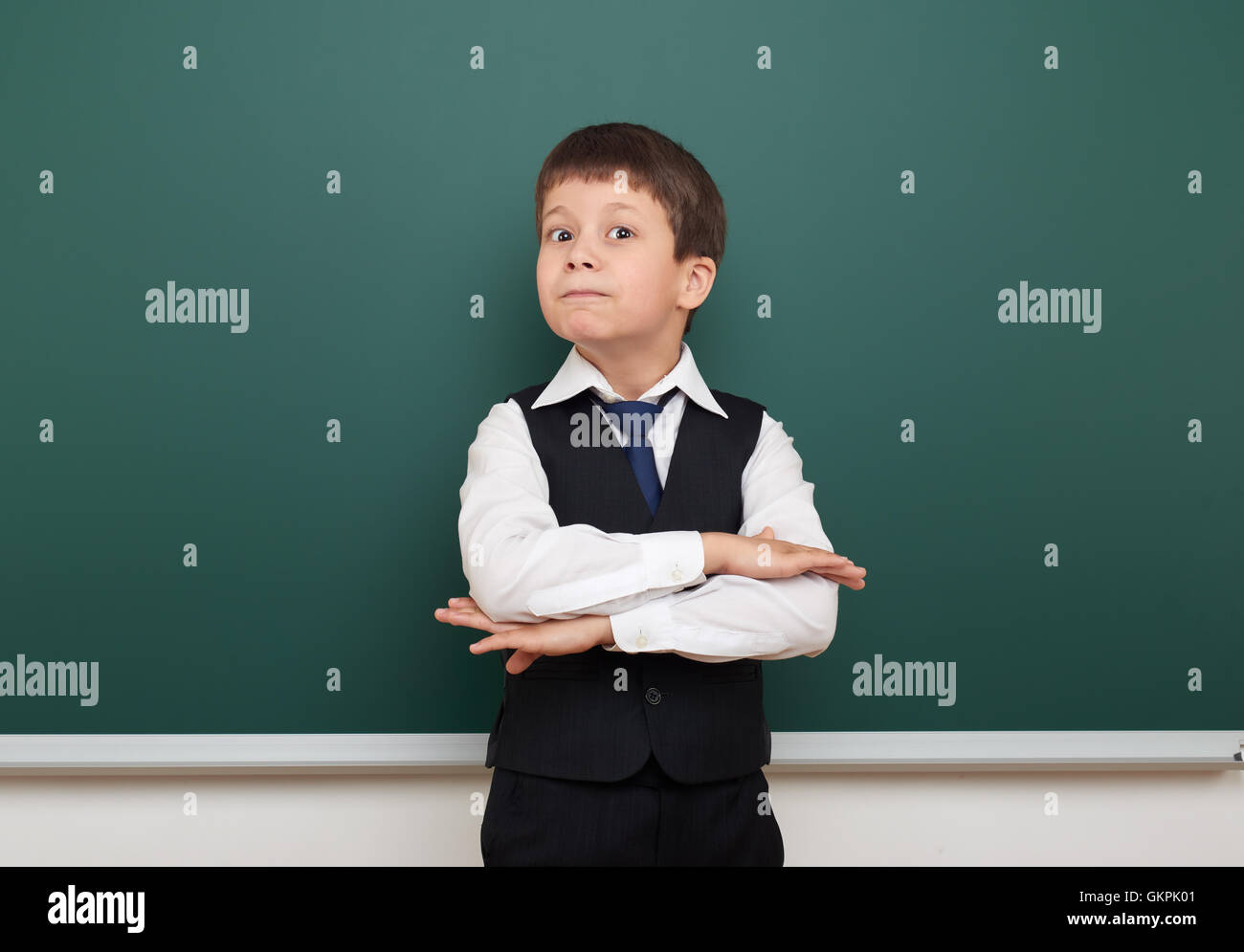 school student boy posing at the clean blackboard, grimacing and ...